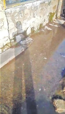 Water flowing wastefully from a broken line in the wall of the post office
