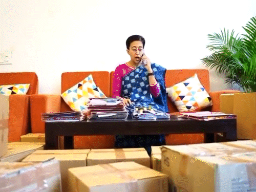 CM Atishi working amidst cartoons full of goods